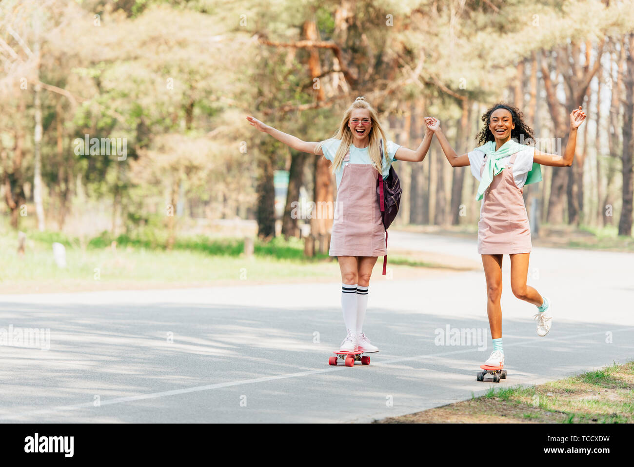 full length view of two smiling multicultural friends holding hands ...