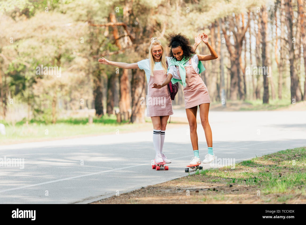 full length view of two smiling multicultural friends skateboarding on ...