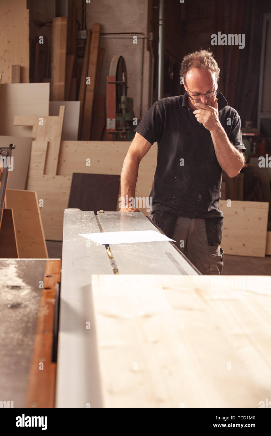 Carpenter or woodworker in his workshop standing looking thoughtfully ...