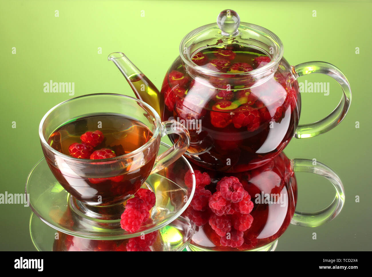 Black fruit raspberry tea in glass teapot and cup on green background ...