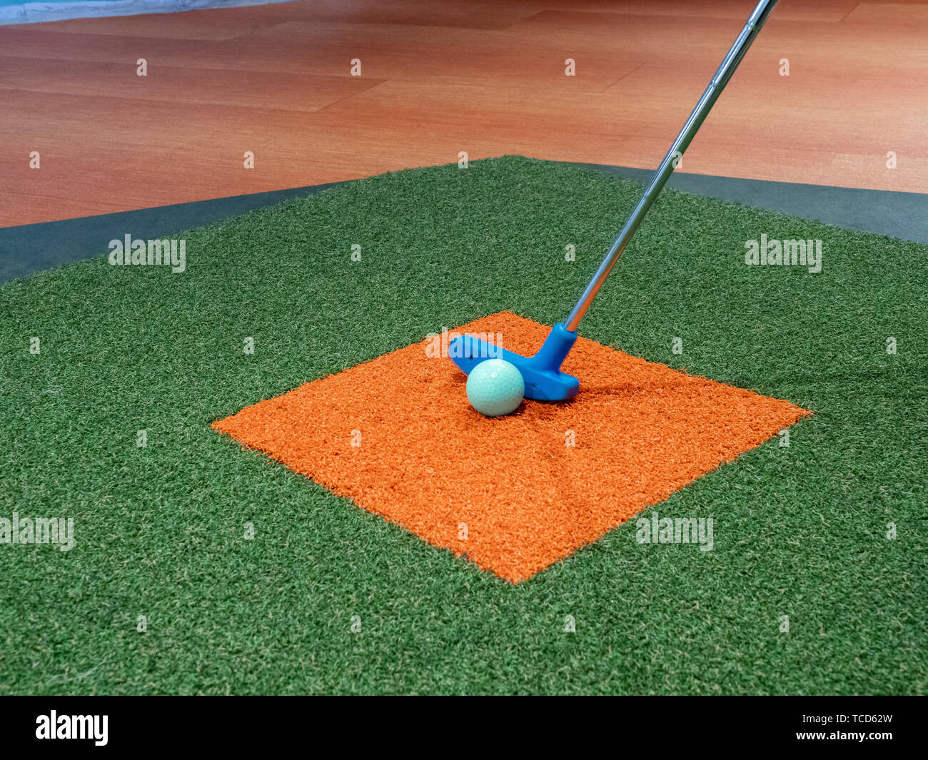 Blue putter on turf lined up next to green golf ball on orange turf on ...