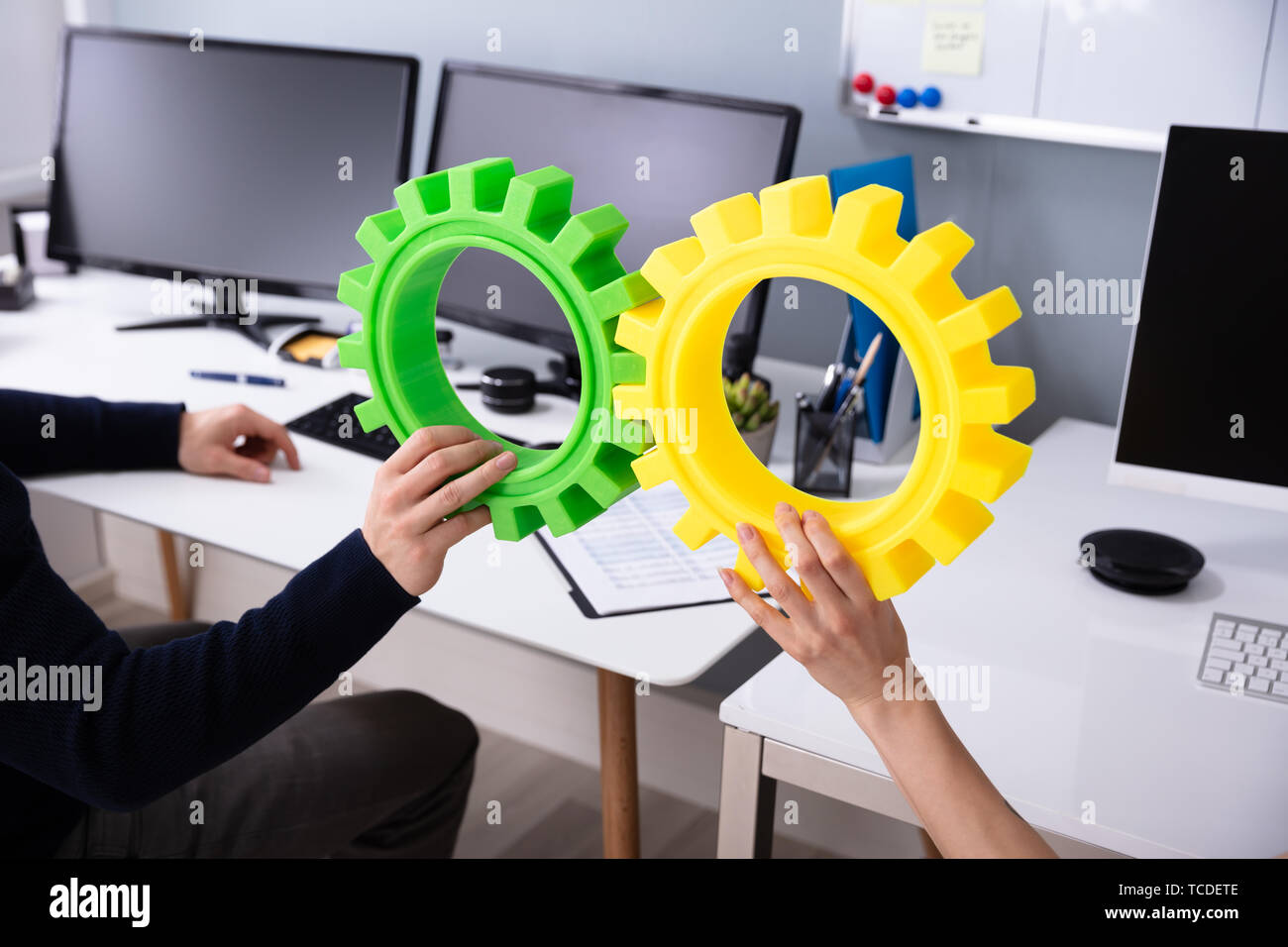 Two Businesspeople's Hand Joining Green And Yellow Gears In Front Of ...