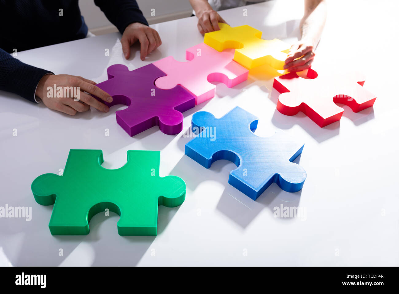 Two Businesspeople Solving Multi Colored Jigsaw Puzzle Over White Desk ...