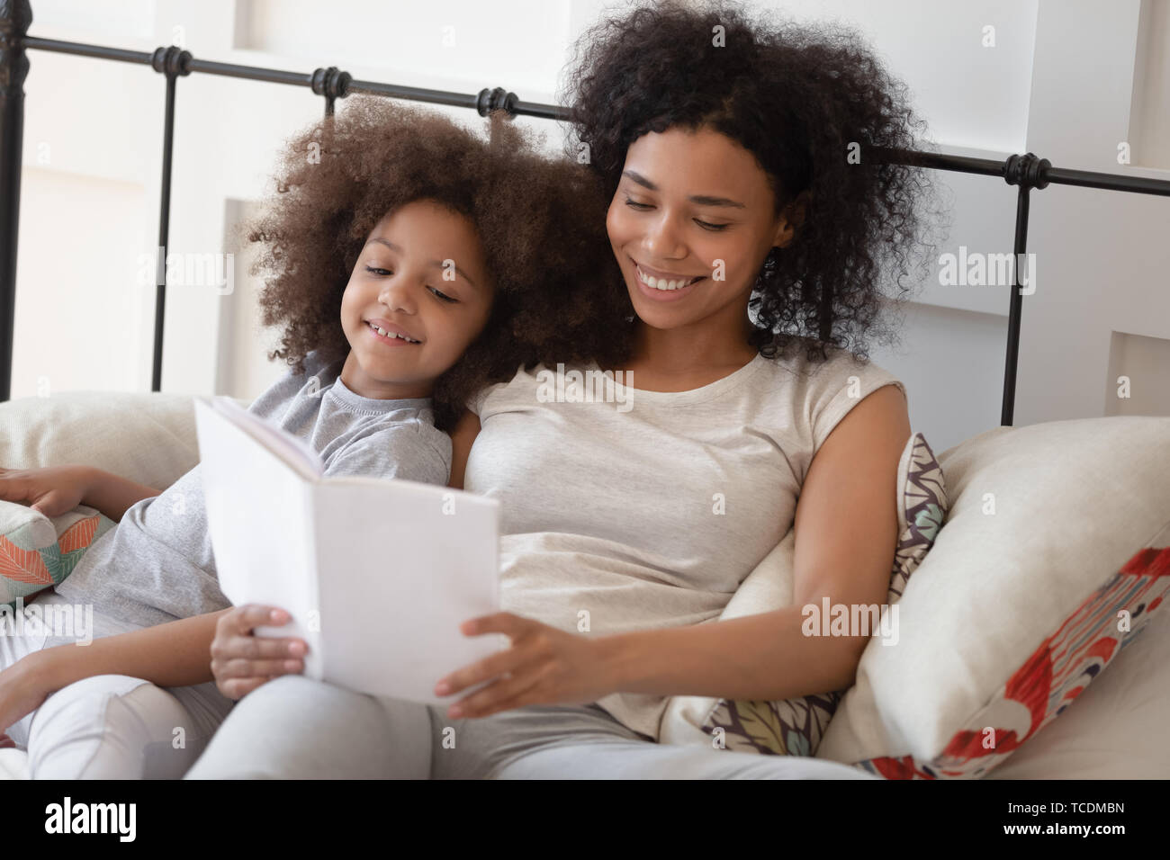 Happy african mother reading book relaxing in bed with daughter Stock ...