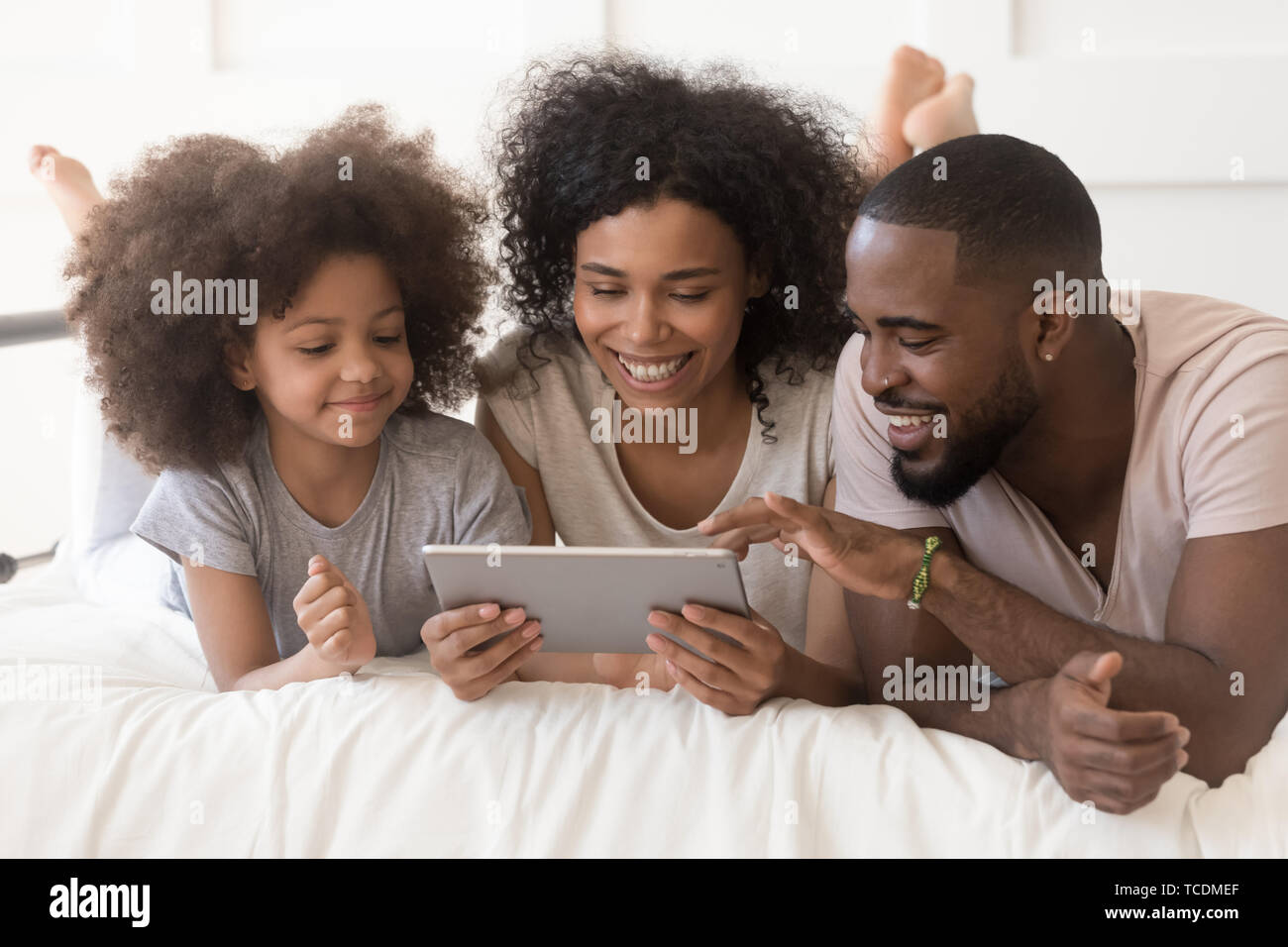 Happy african parents with daughter using tablet lying on bed Stock ...