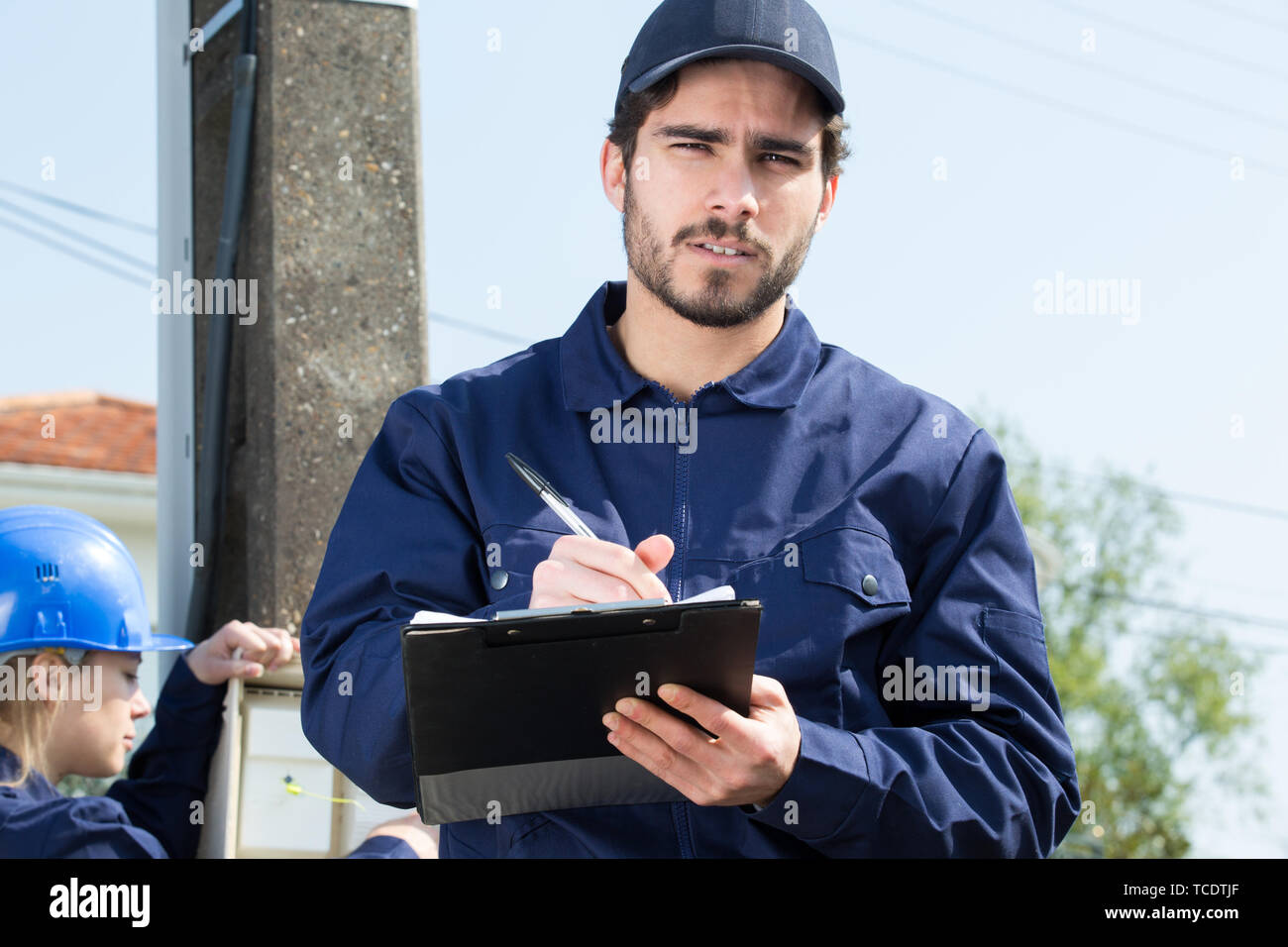 engineer in blue overall writing on clipboard by electric meter Stock Photo - Alamy