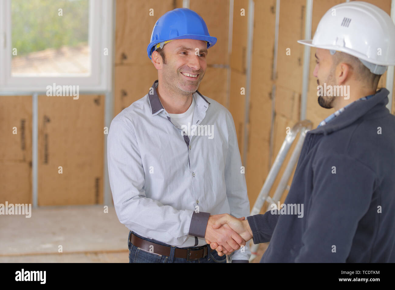young male architect and construction worker shaking hands Stock Photo ...