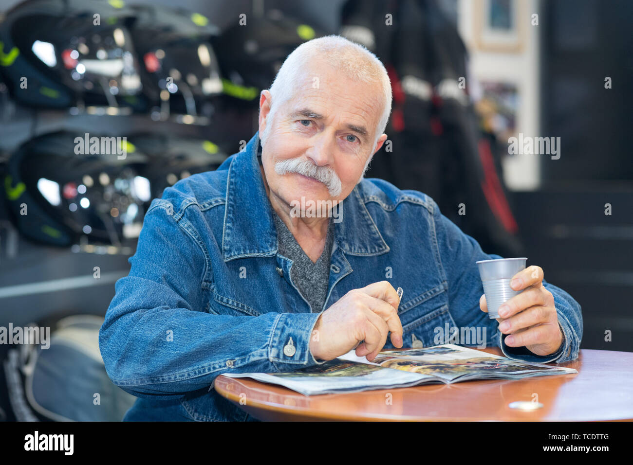 senior man drinking coffee and reading magazine in motorcycle store ...