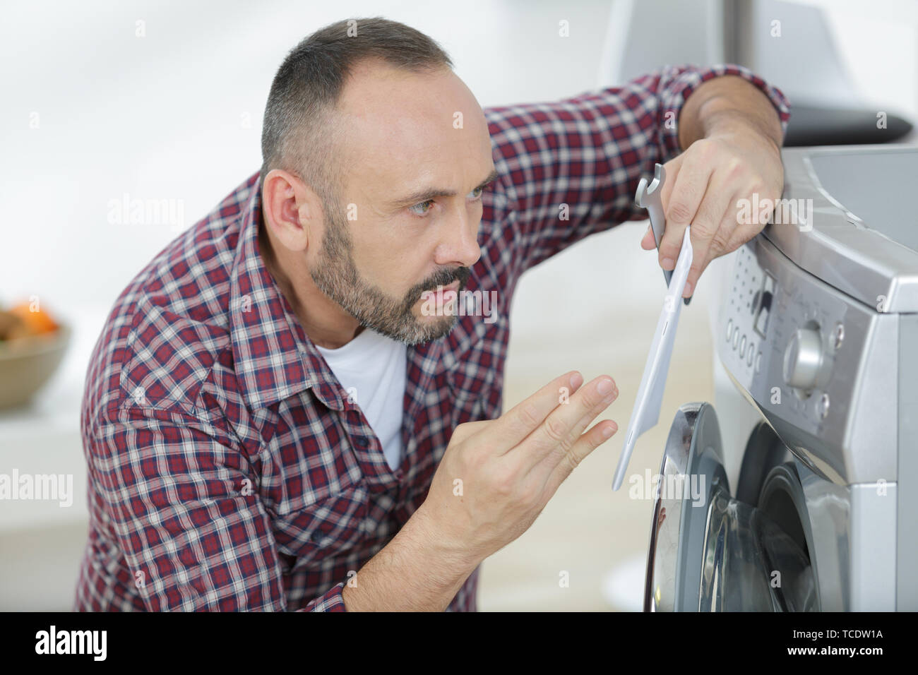 man looking at washing machine and holding instructions Stock Photo - Alamy