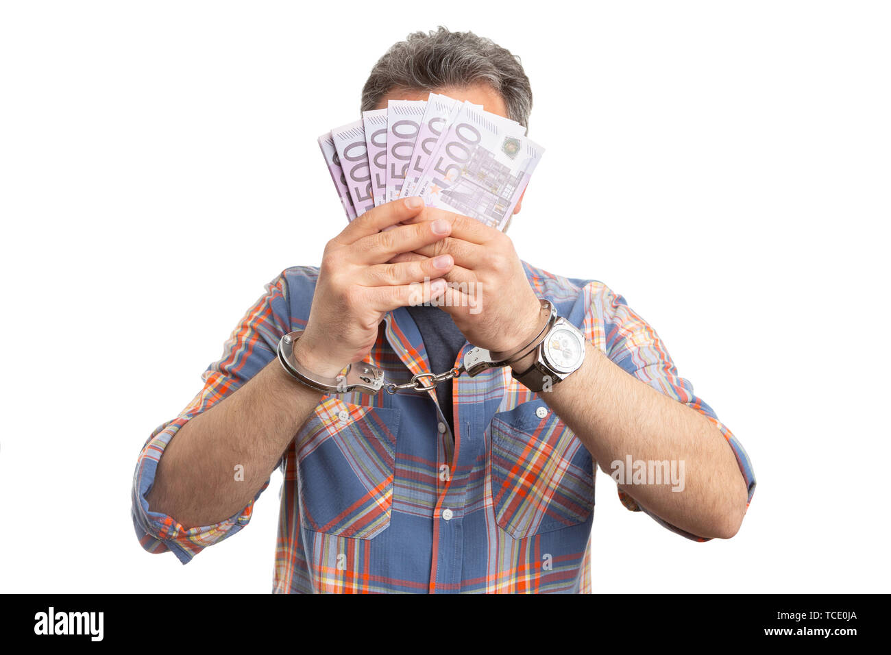 Corrupted man covering face with money bills and handcuffed hands as ...