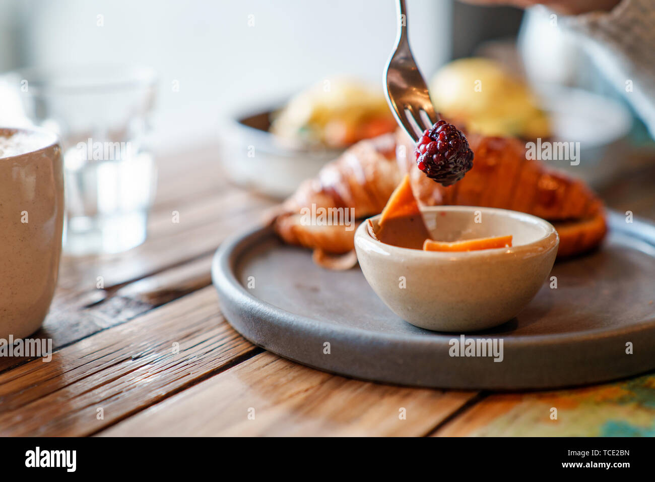 Breakfast croissant with coffee and a person eating blackberry garnish ...