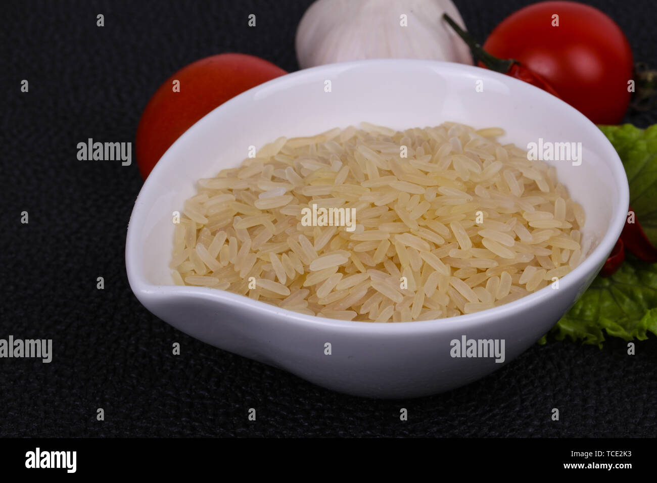 Raw uncooked rice in the bowl served pepper and salad leaves Stock ...