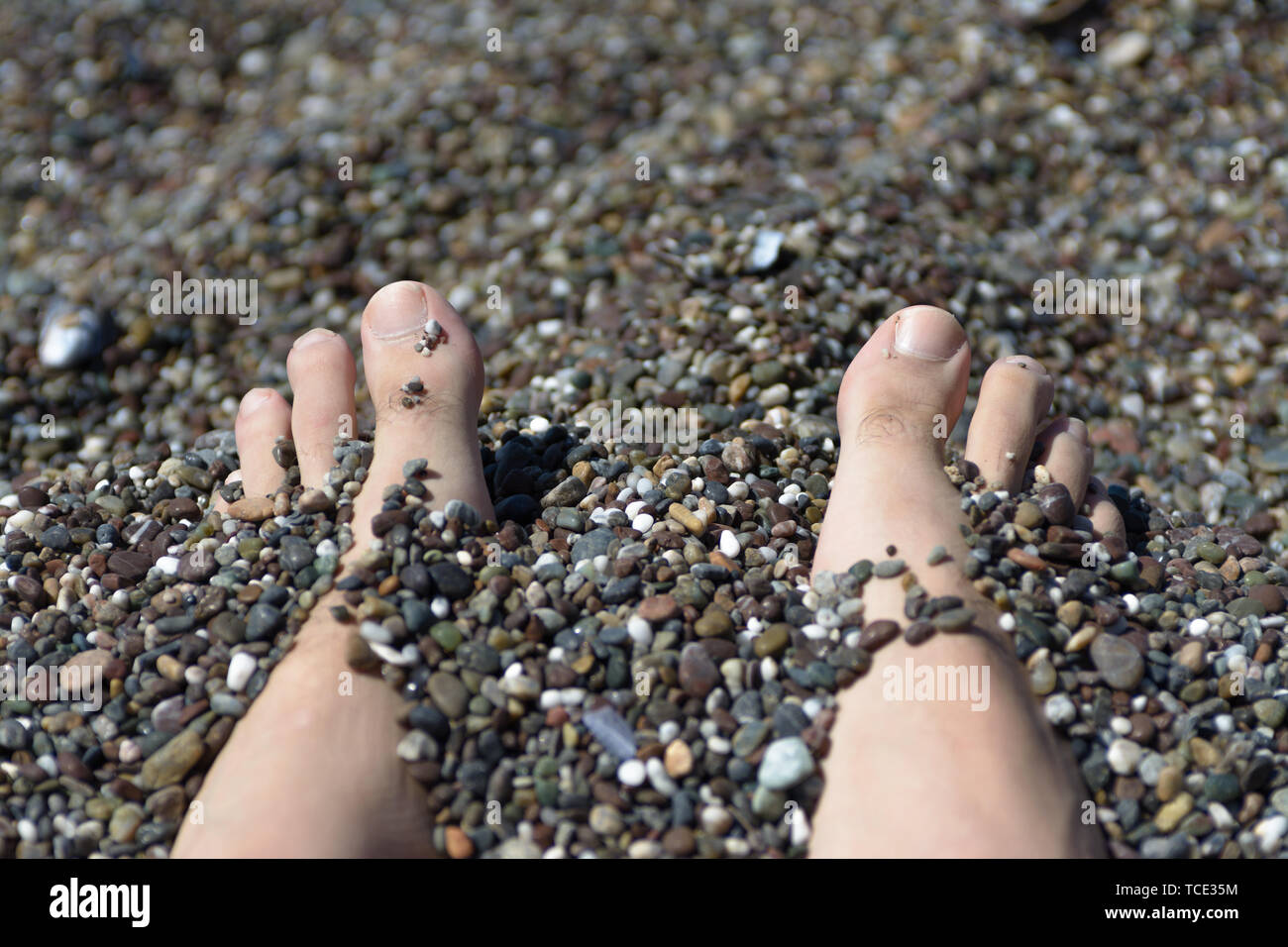 Feet and toes buried in the stone sand of this beach. Many colors Stock ...