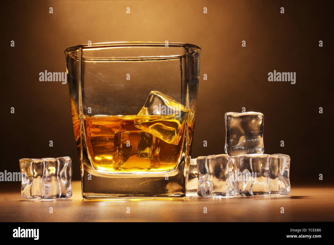 glass of scotch whiskey and ice on wooden table on brown background ...