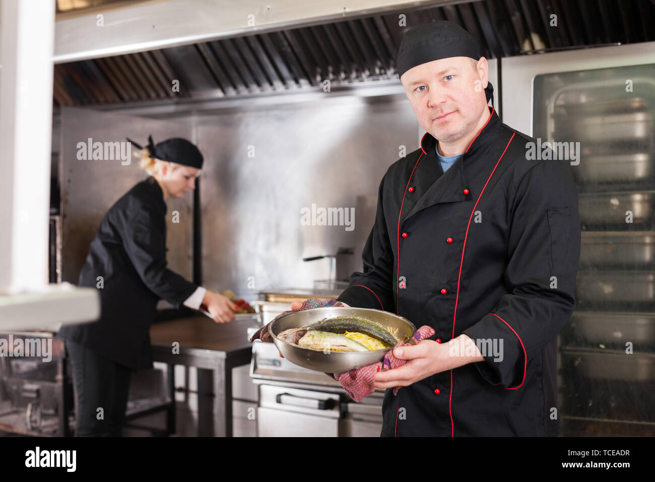 Skilled cook offering to taste just prepared baked fish with vegetables ...