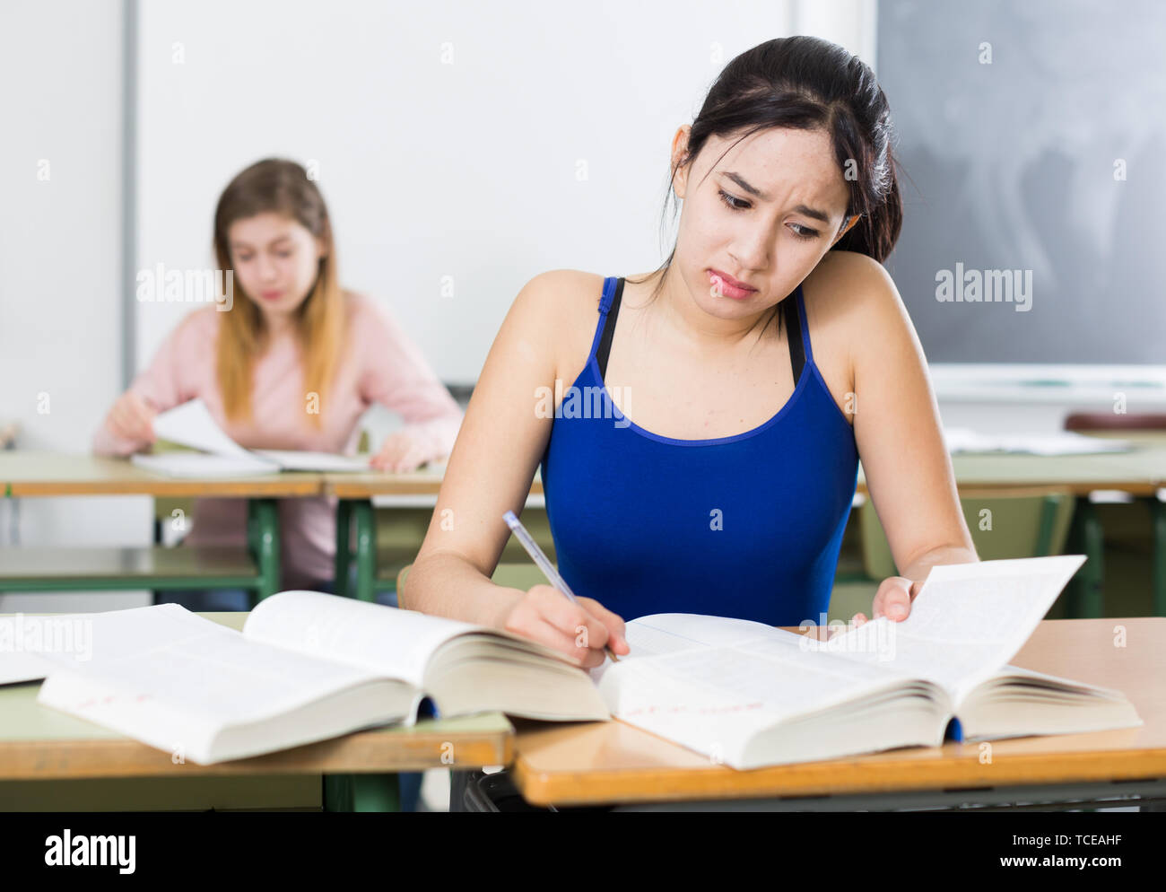 Portrait schoolgirl who is solving a difficult task at the desk in the ...