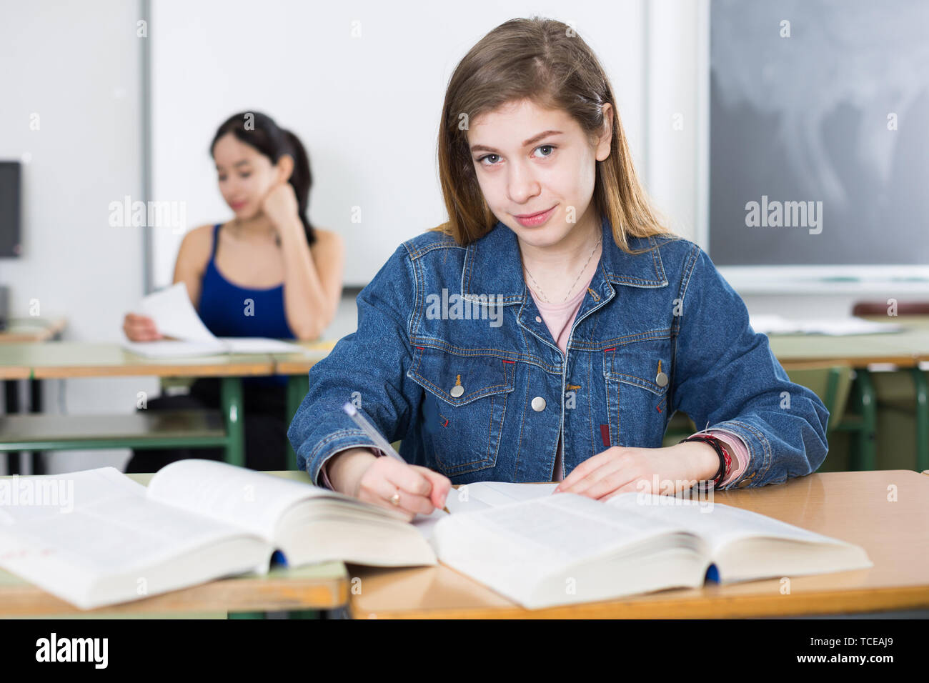 Young girl is sitting at the desk and reading text in the classroom in ...