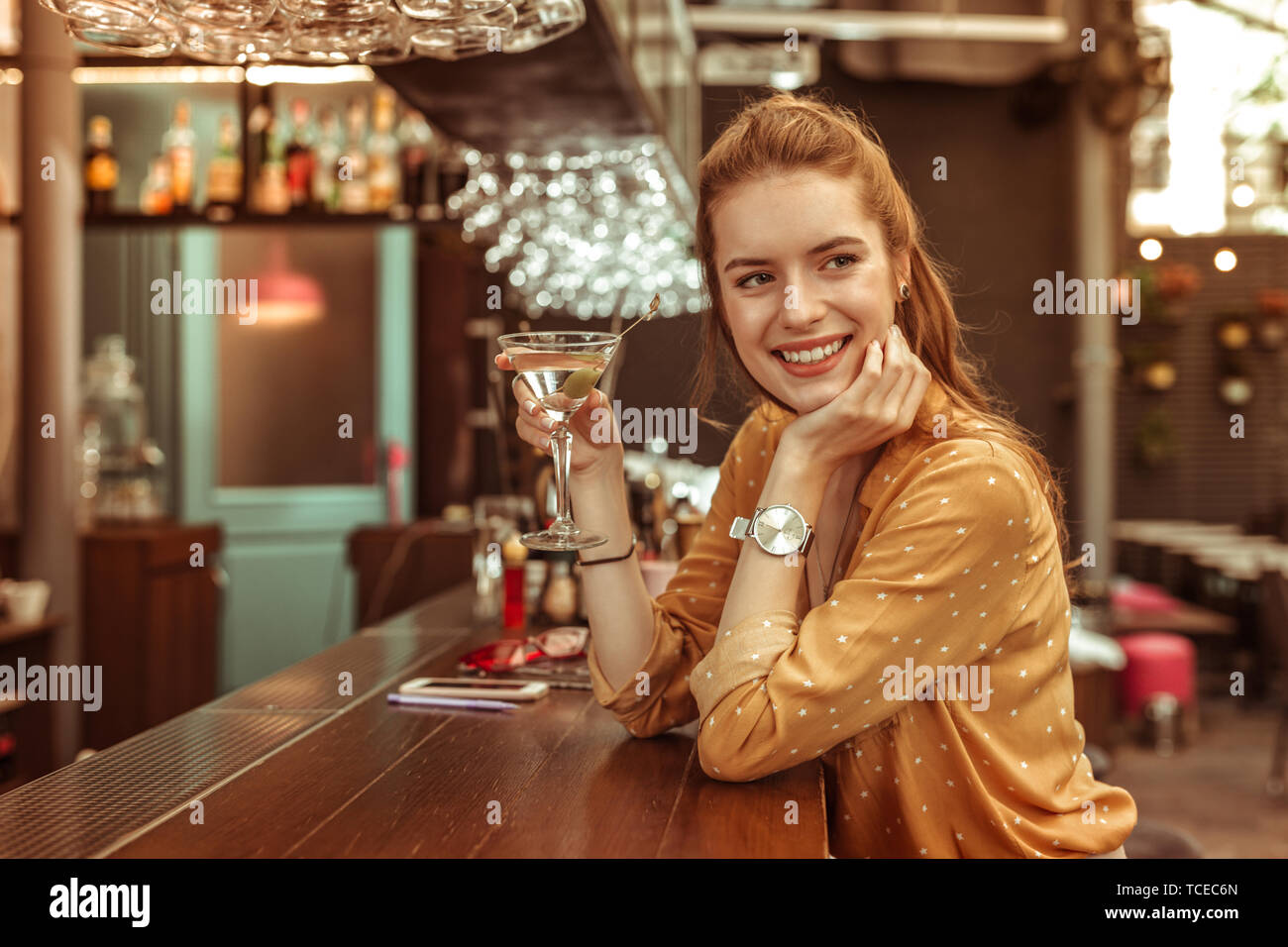 Holding a drink. Smiling glowing happy contended red-haired appealing ...