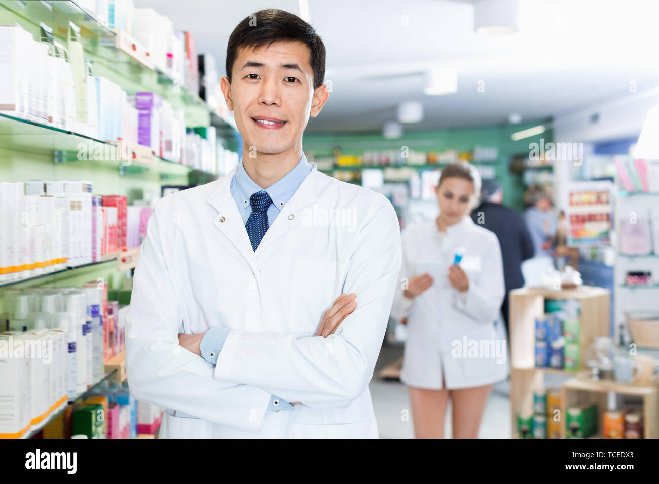 Portrait of chinese positive man pharmacist who is standing on his work ...