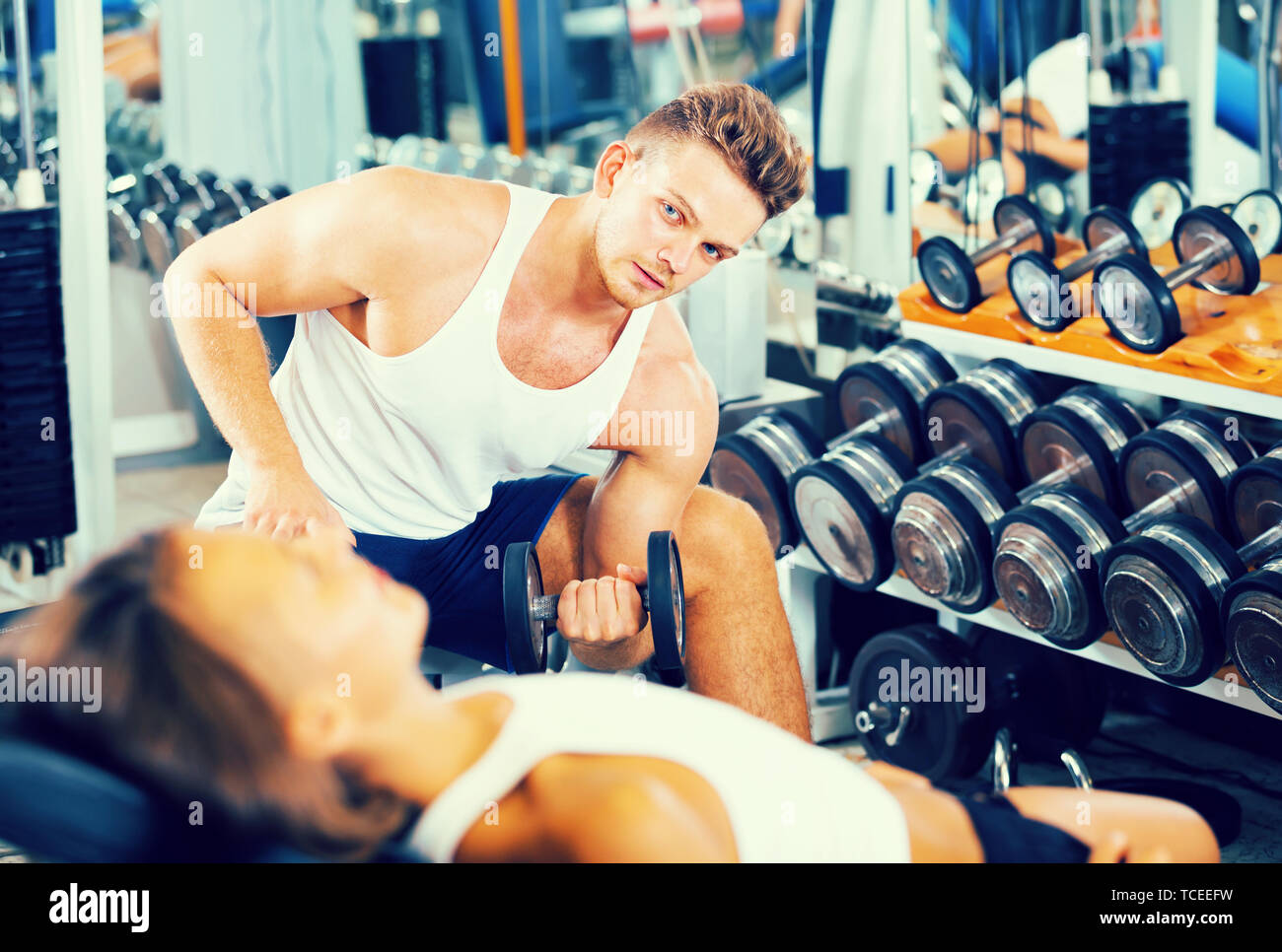 Young positive man making biceps curls using heavy dumbbells in gym ...