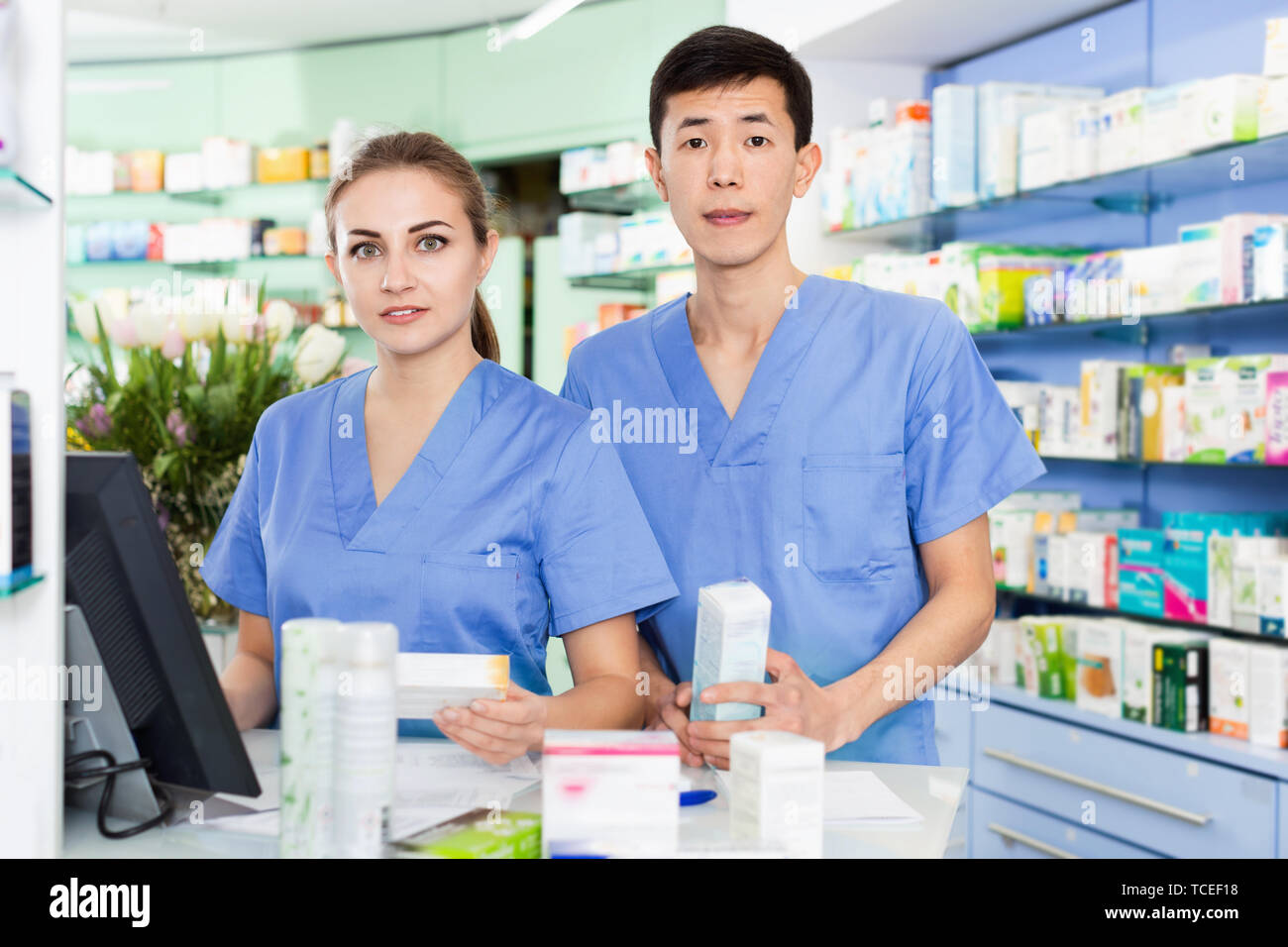Efficient man and woman pharmacists are posing near table with cashbow ...