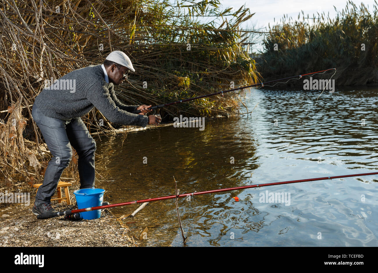 Portrait of afro fisherman standing near river and fishing with rod ...
