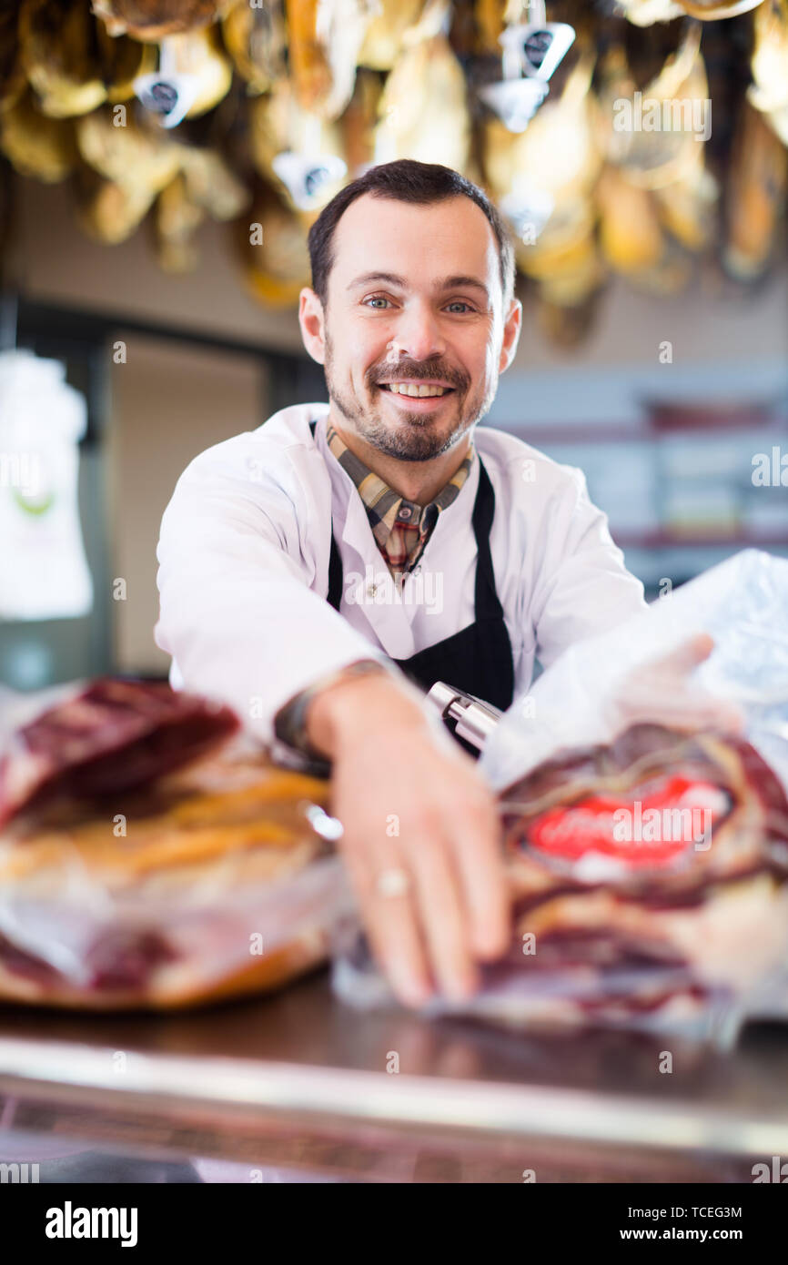 Male Shop Assistant Demonstrating Sorts Of Meat In Butchers Shop Stock