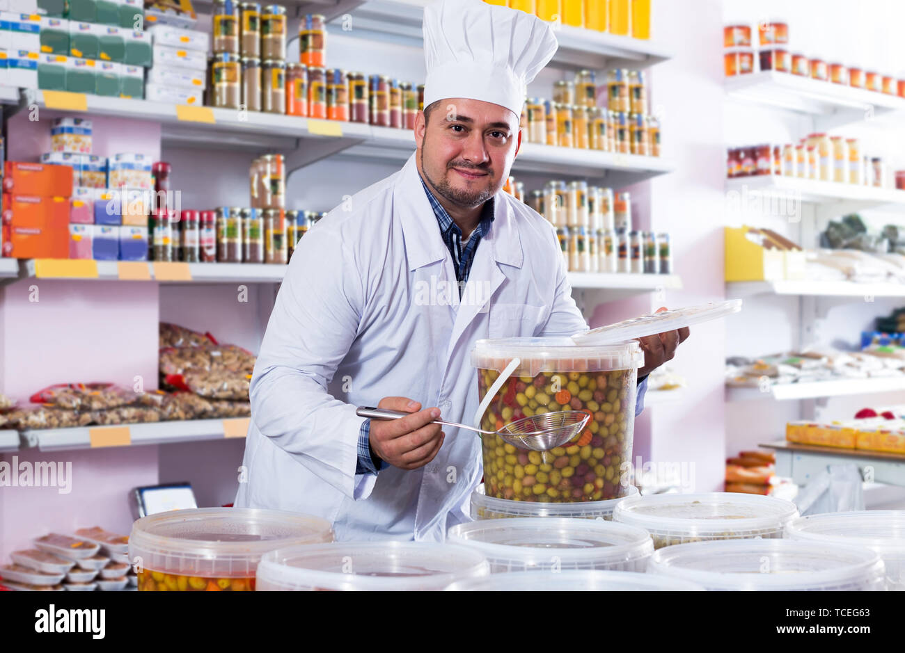 happy shop staff standing near containers with olives in flavoured ...