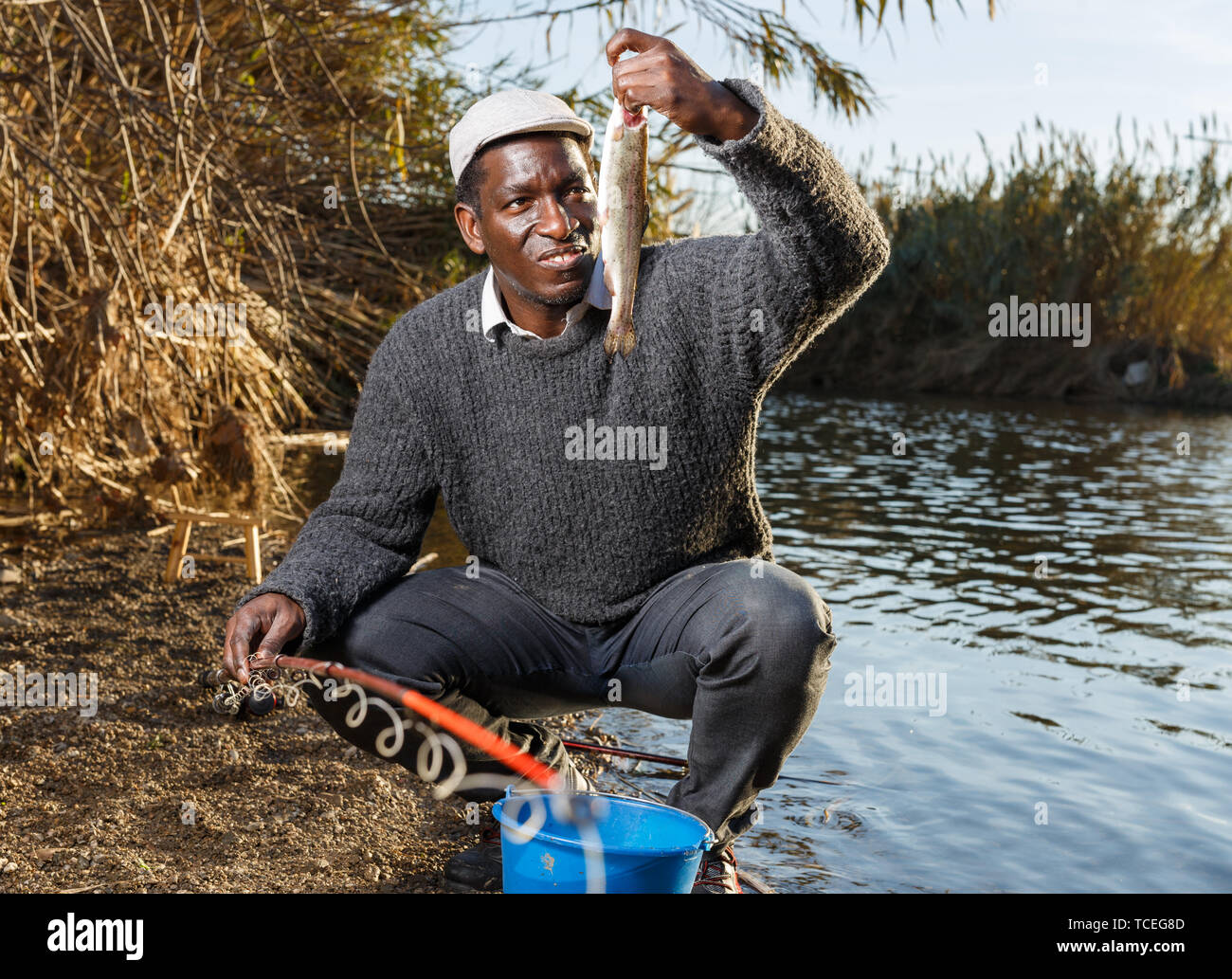Portrait of African man fishing on river and putting caught fish in ...