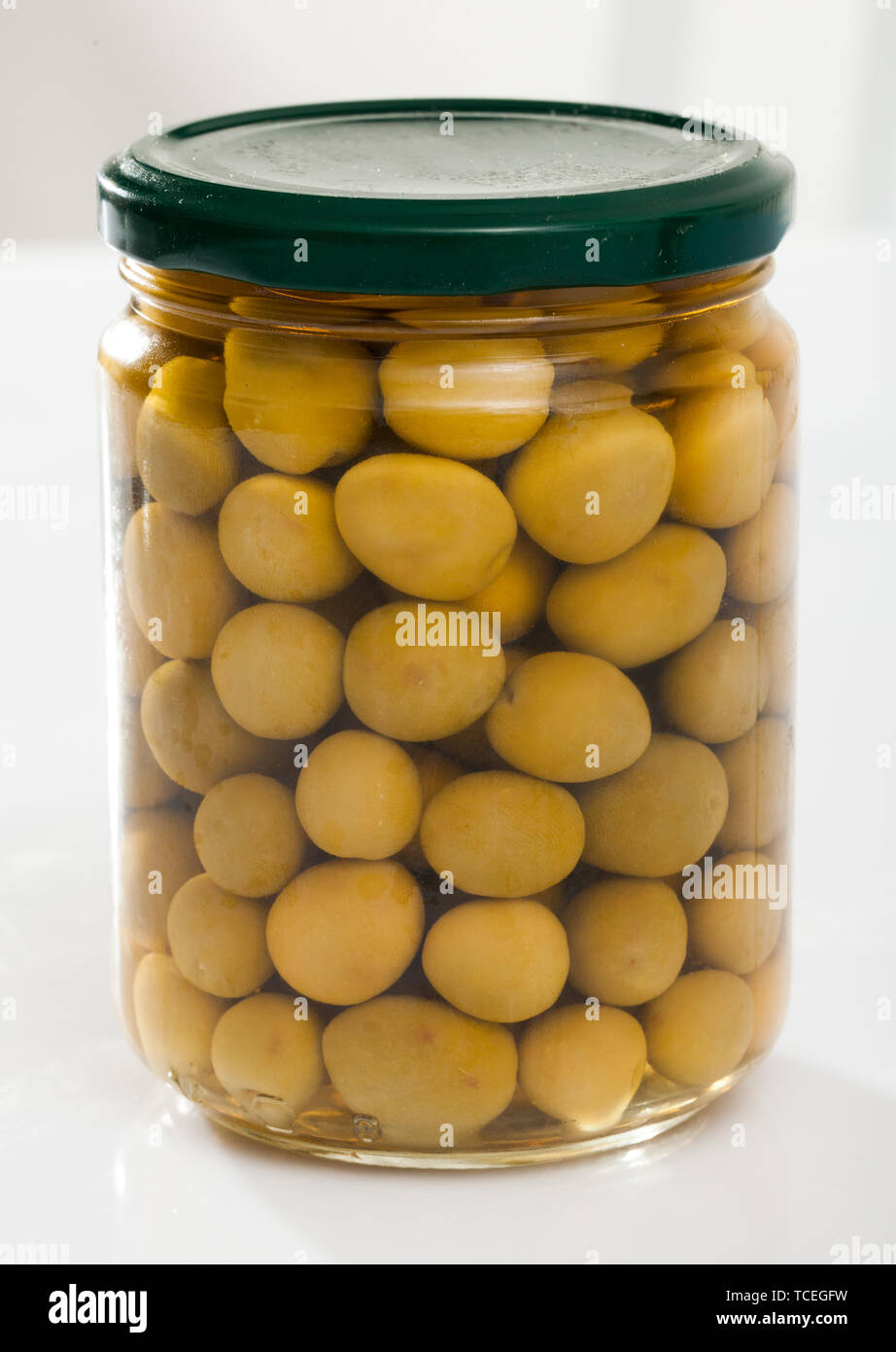 Marinated whole green olives in glass jar on white surface. Organic ...