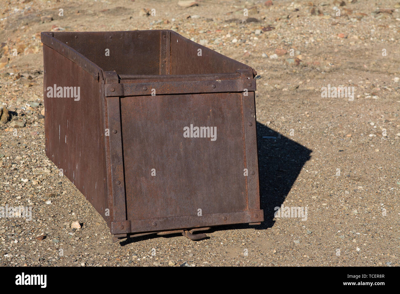 Rusty aged metal box lying on dry desert land in small rocks in ...