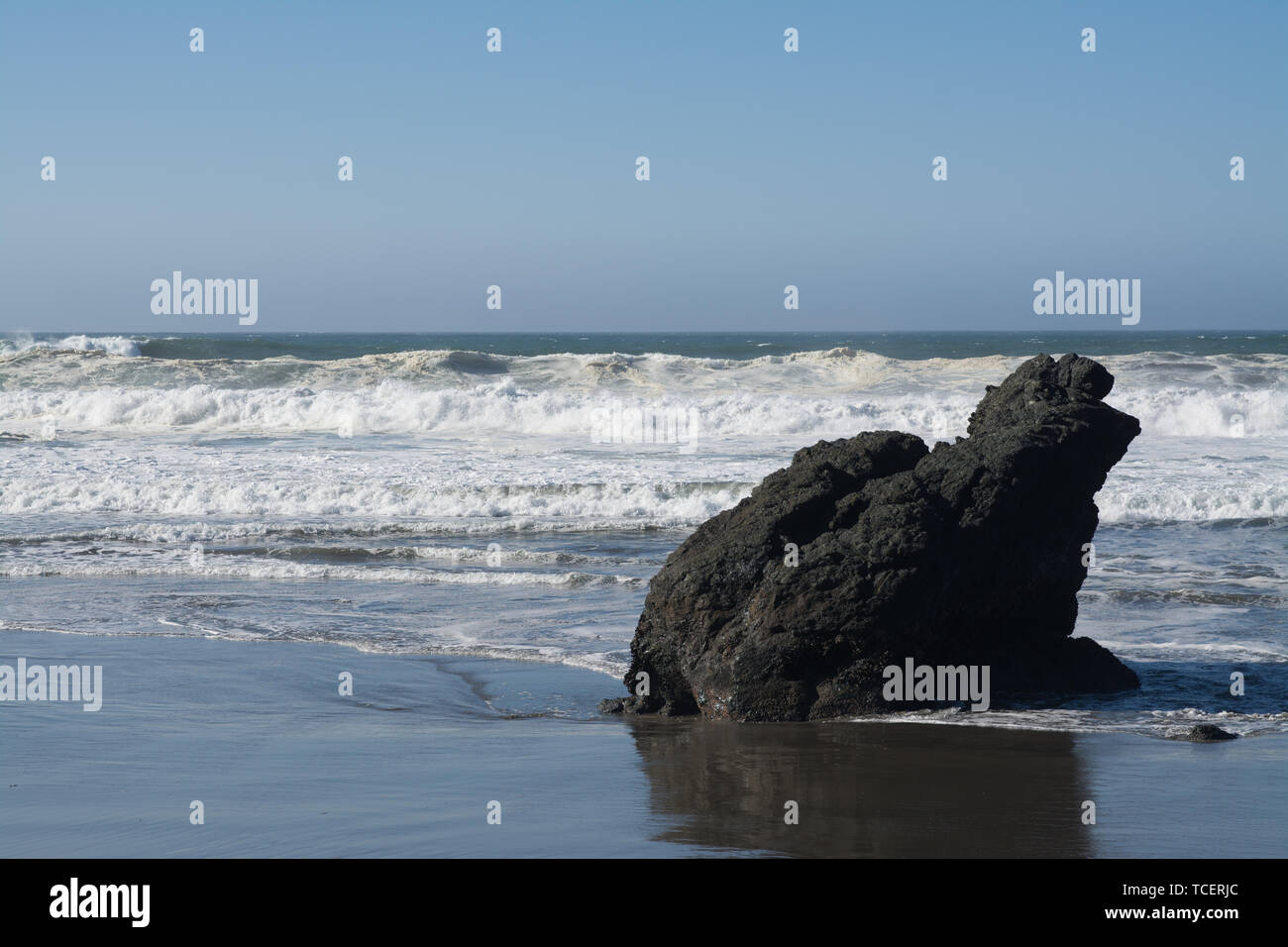View of rough black rock lying on sandy beach with white huge waves of ...