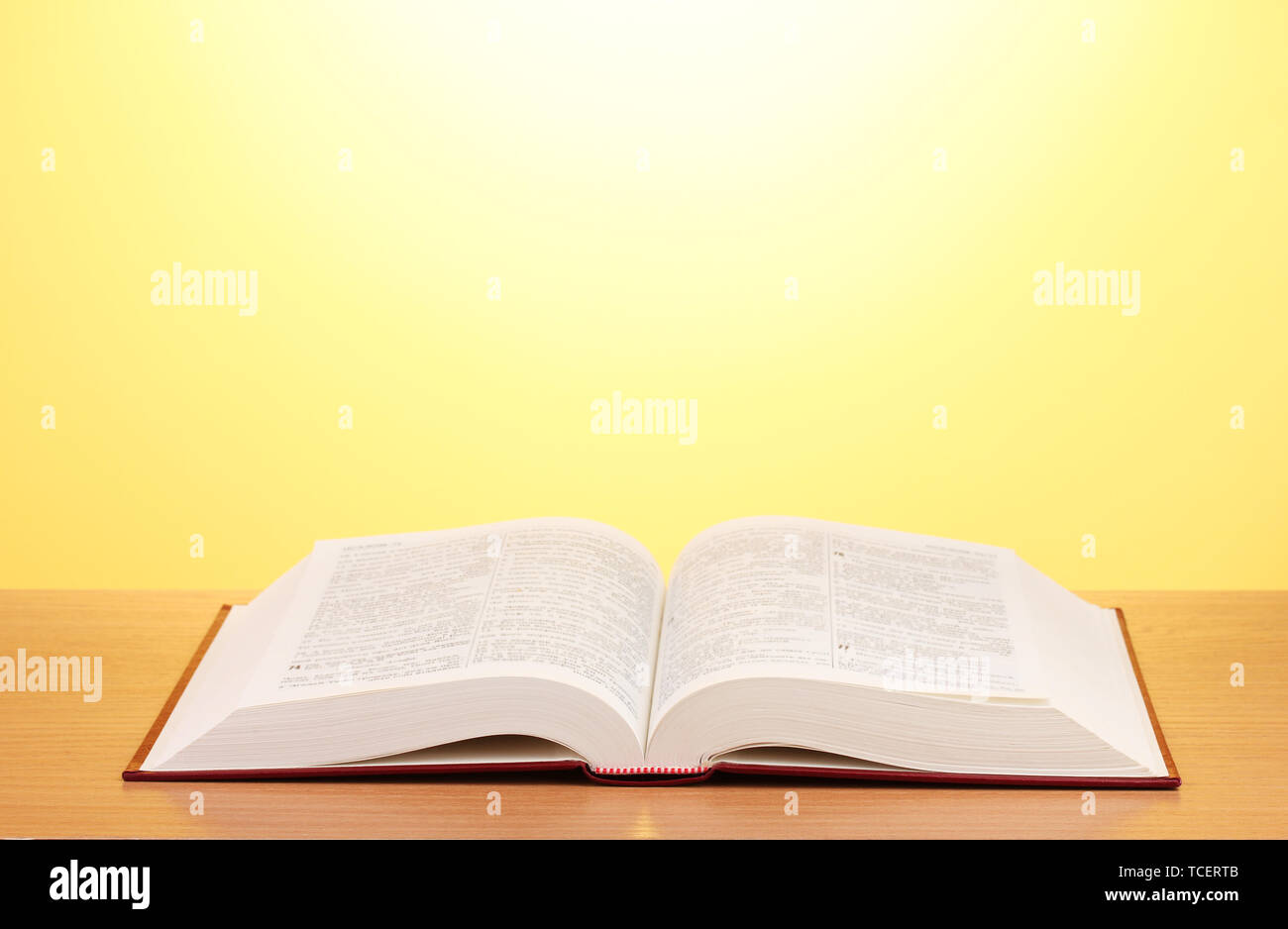 Open book on wooden table on yellow background Stock Photo - Alamy