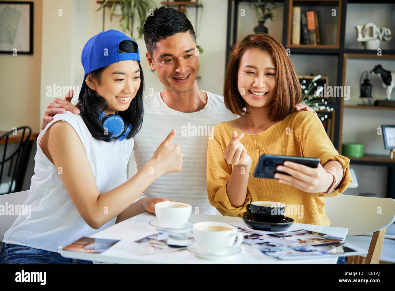 Group of hugging friends sitting at cafe table and smiling and posing ...