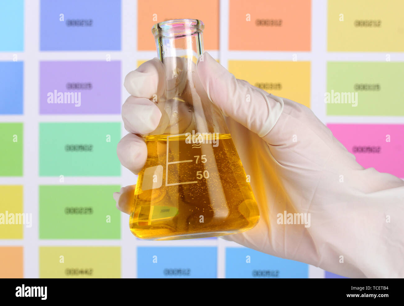 Flask with yellow liquid in hand on color samples background Stock ...