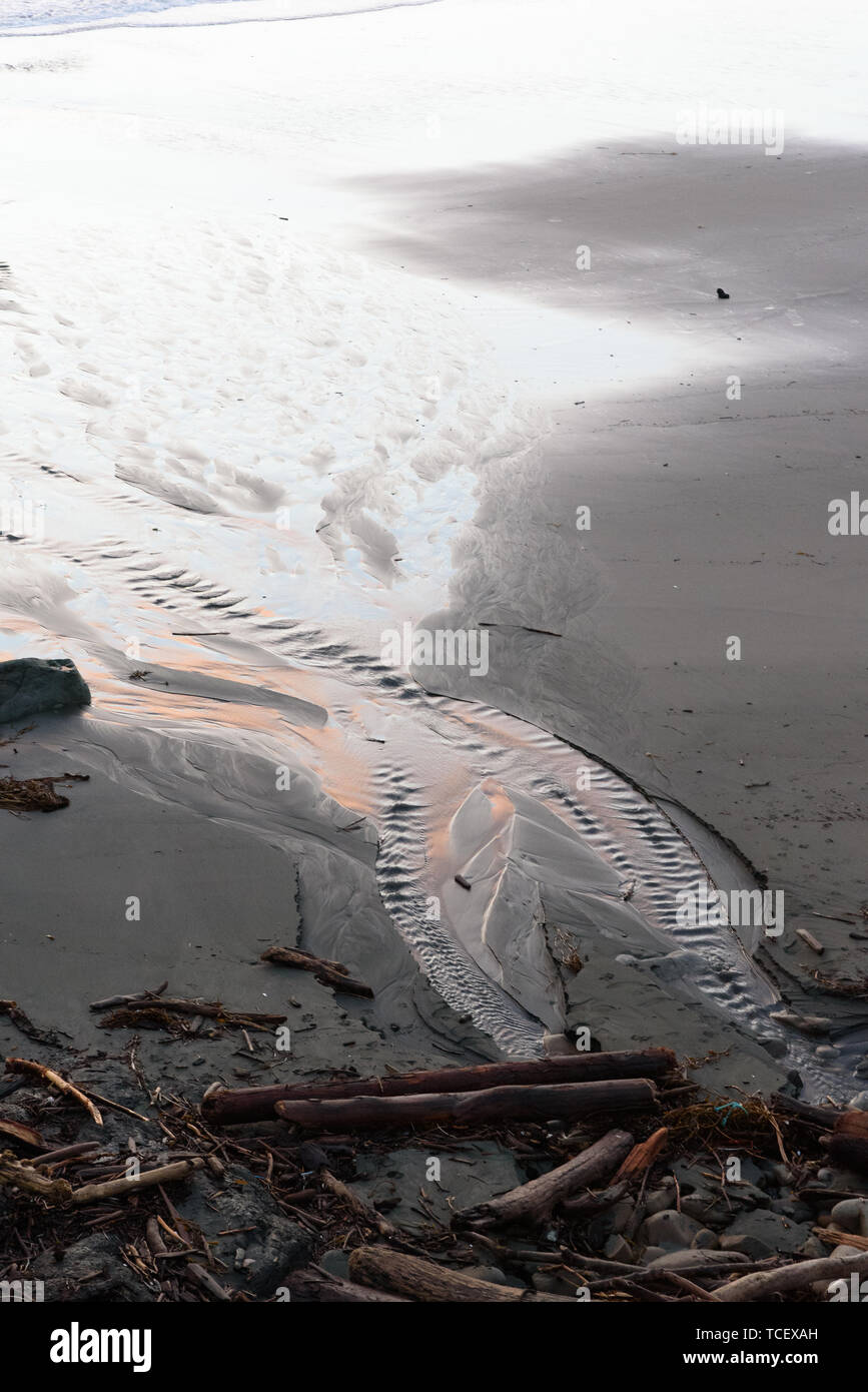 Small stream of clean water flowing on dirty sand of coast towards sea ...