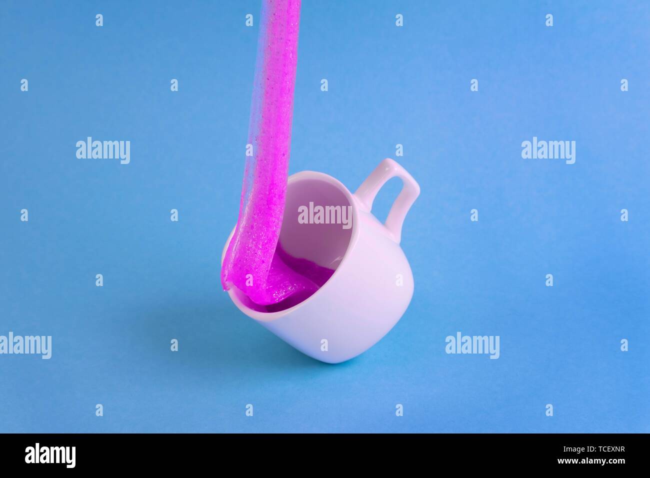 Bright pink glitter slime comes in mug. White cup on blue background ...