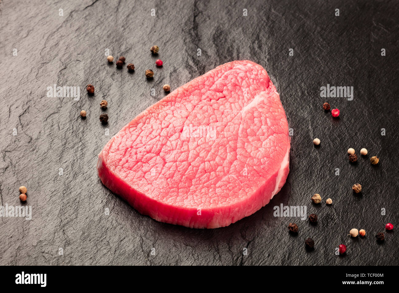 A photo of a steak of eye round beef, a raw cut, with pepper on a black ...
