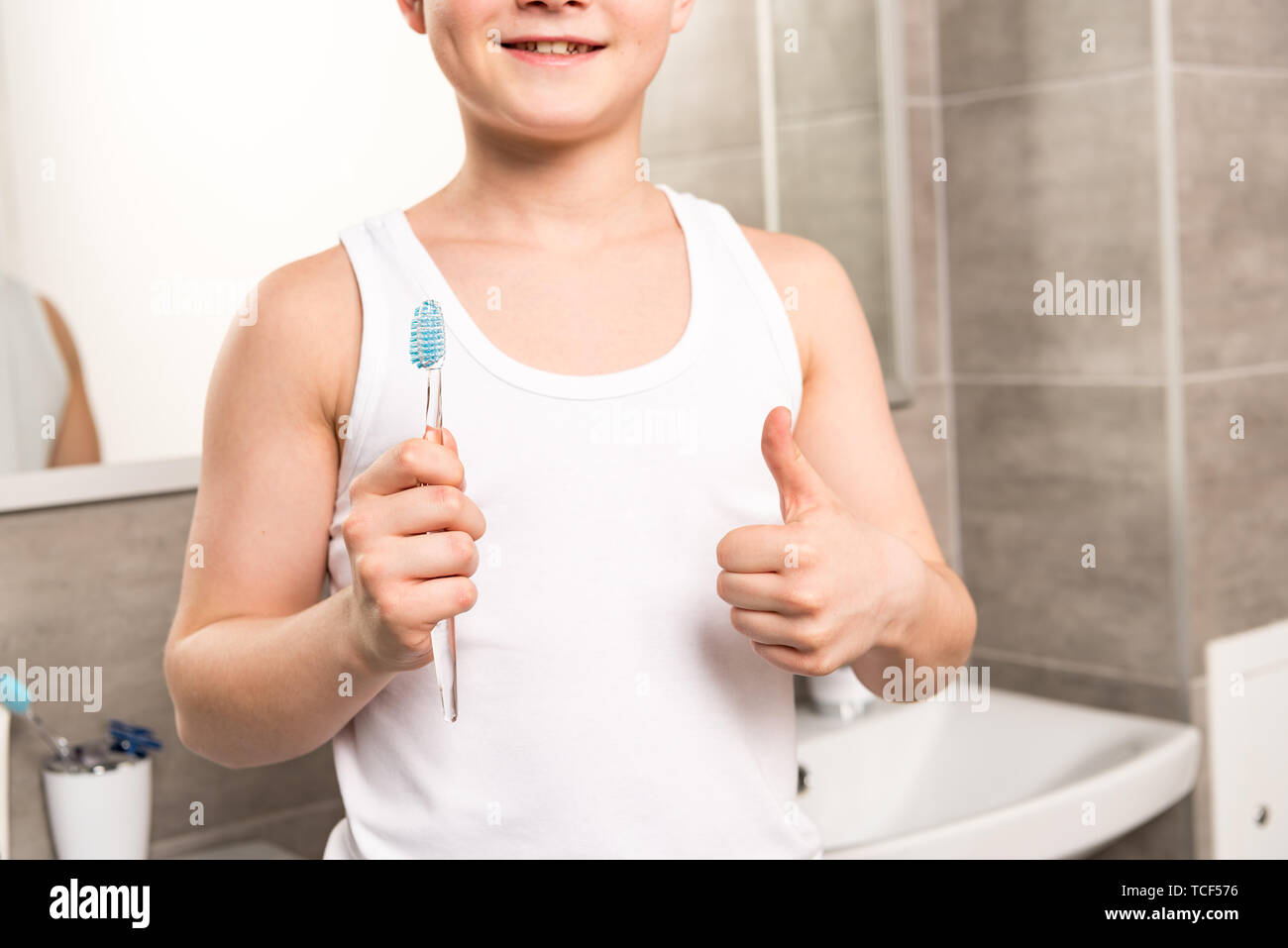 partial view of smiling boy holding toothbrush and showing thumb up in ...