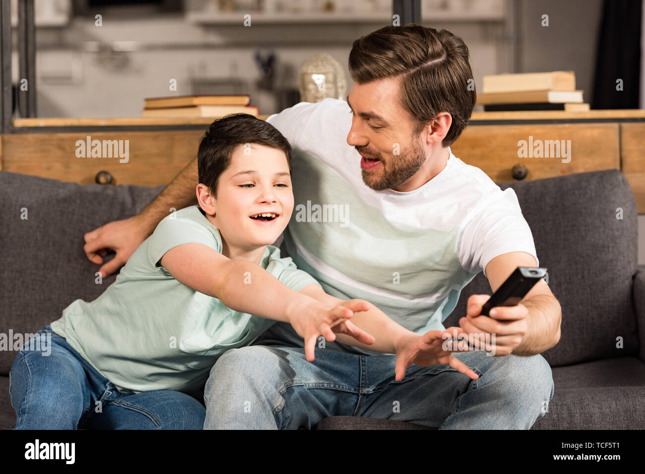 smiling son and father with remote controller watching tv in living ...