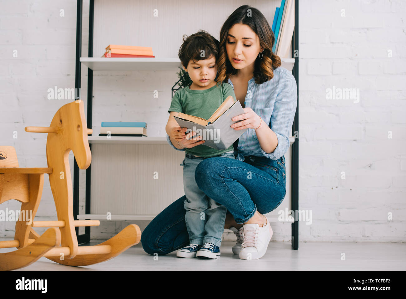 Mother and child reading book in living room Stock Photo - Alamy