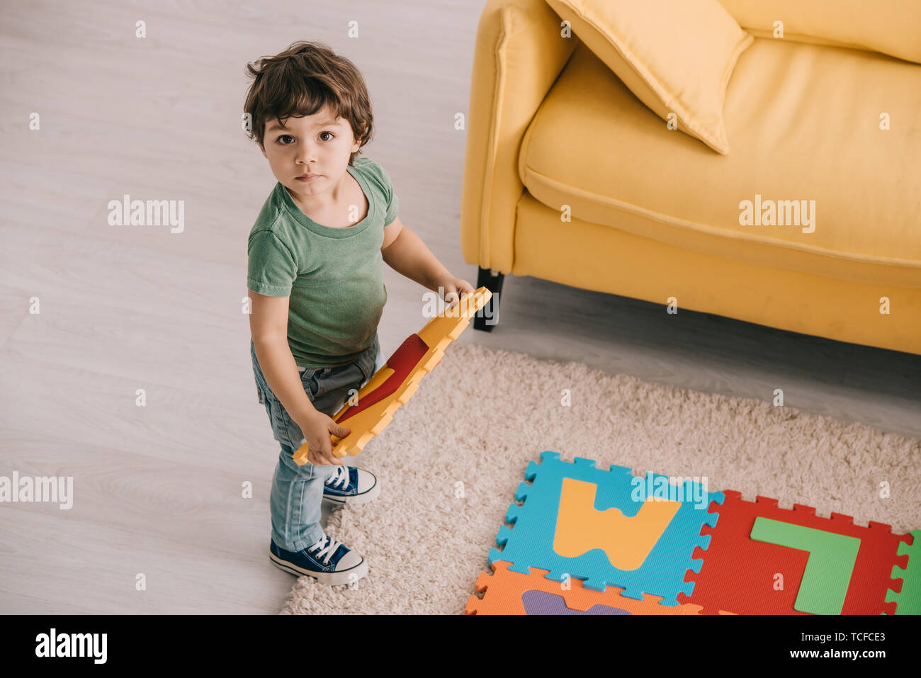overhead view of cute child in green t-shirt playing with puzzle mat ...