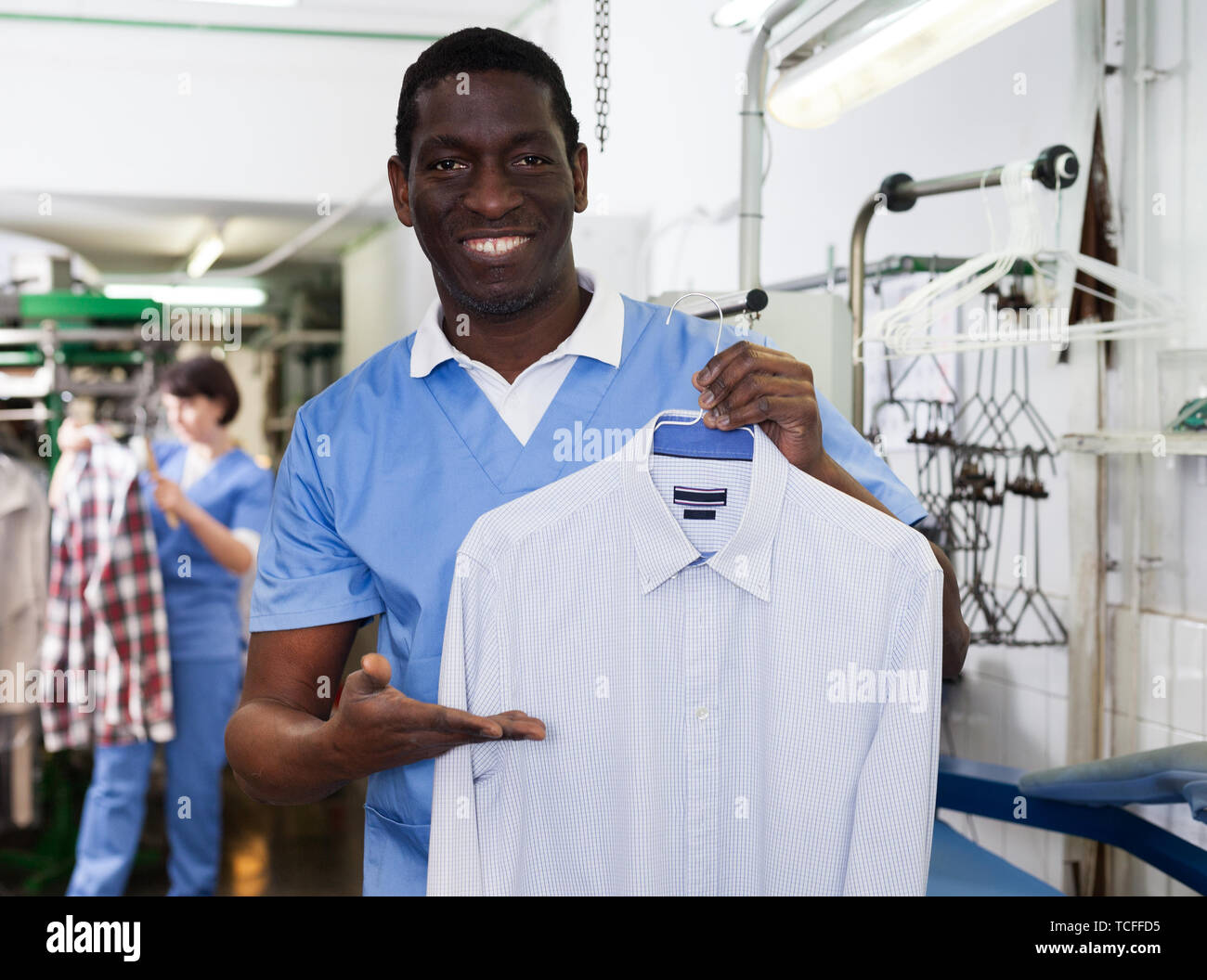 Cheerful African American man worker of dry cleaner showing clean ...