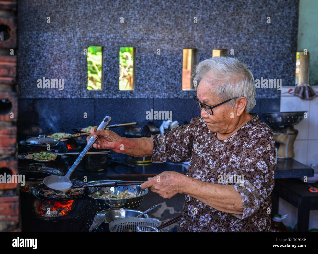 An old woman cooking traditional seafood pancake at old kitchen in Nha ...
