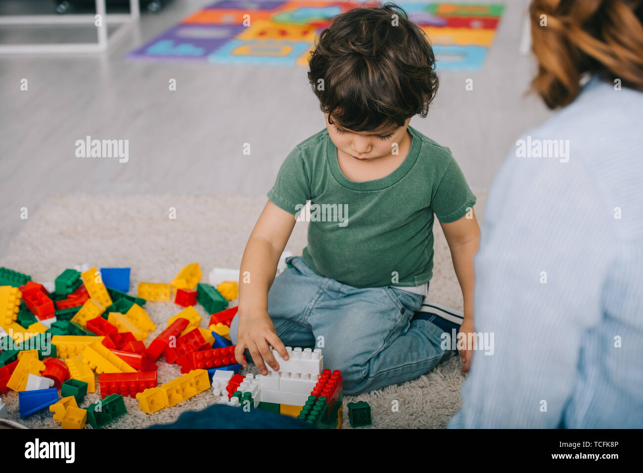 cropped view of mother and son playing with lego on carpet in living ...