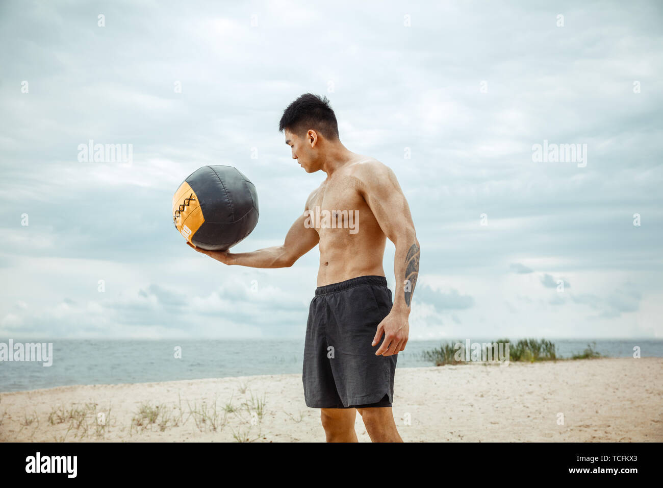 Young healthy man athlete doing exercise with ball at the beach. Signle ...