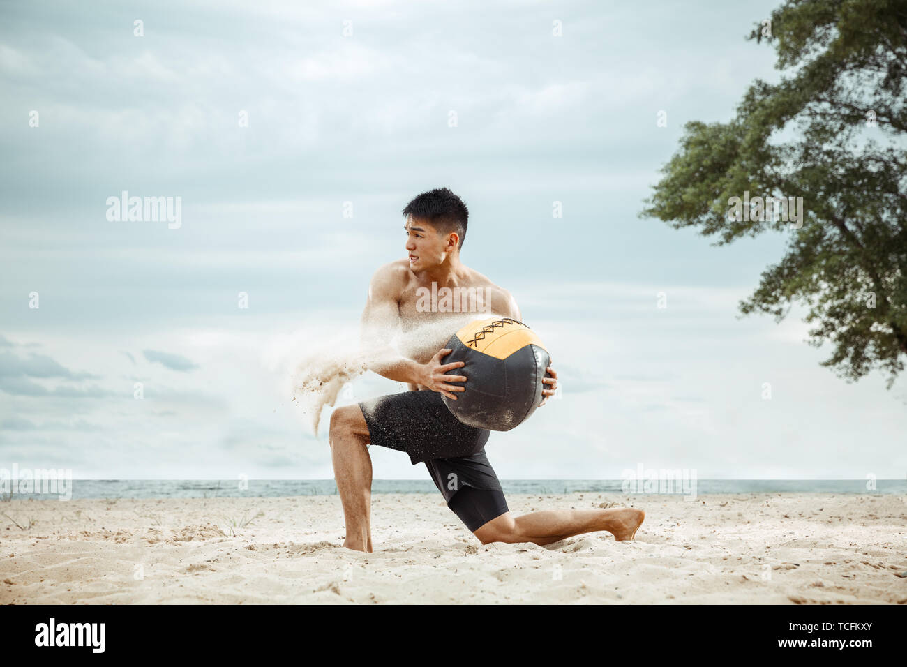 Young healthy man athlete doing exercise with ball at the beach. Signle ...