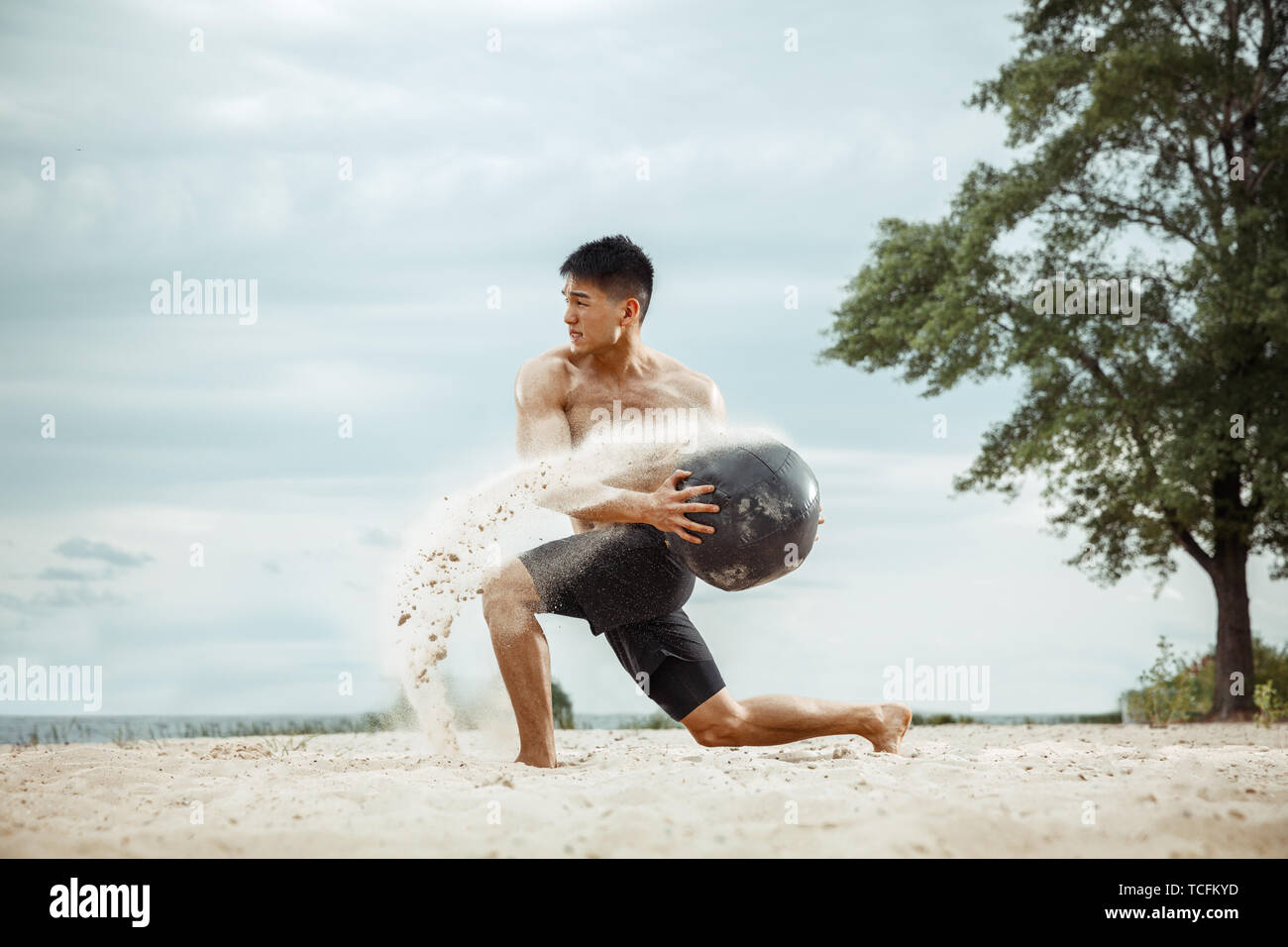 Young healthy man athlete doing exercise with ball at the beach. Signle ...