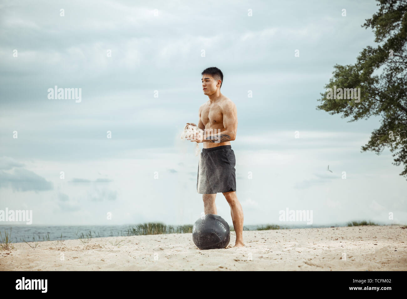 Young healthy man athlete doing exercise with ball at the beach. Signle ...