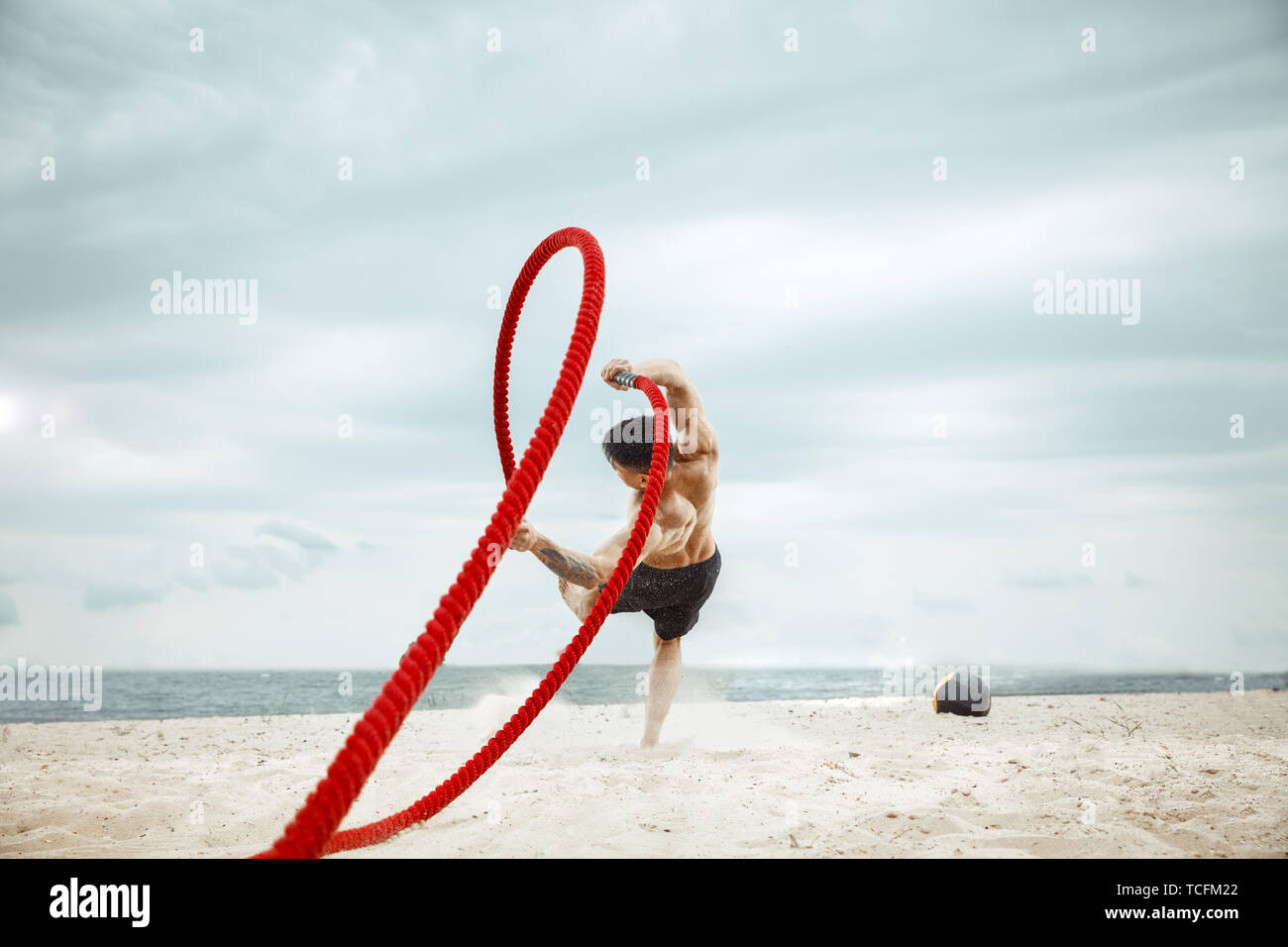 Young healthy man athlete doing exercise with the rope at the beach ...